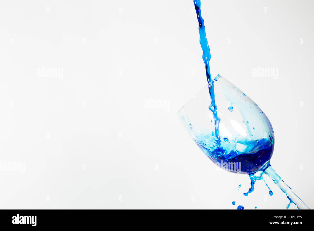 A stream of poured bright blue liquid splashes into a tilted clear wine ...