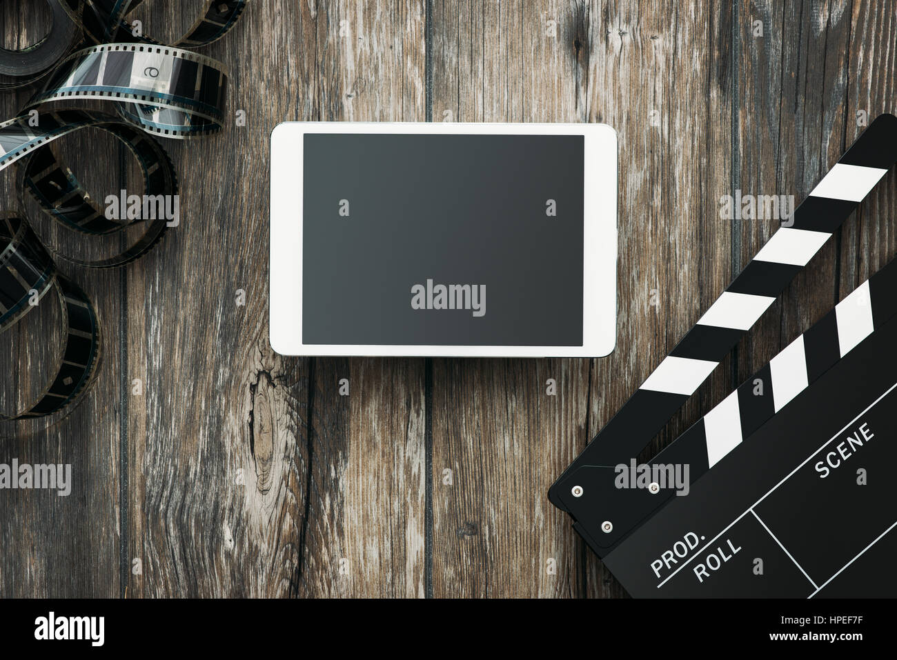 Digital tablet, clapper and filmstrip on a wooden desktop: cinema and ...