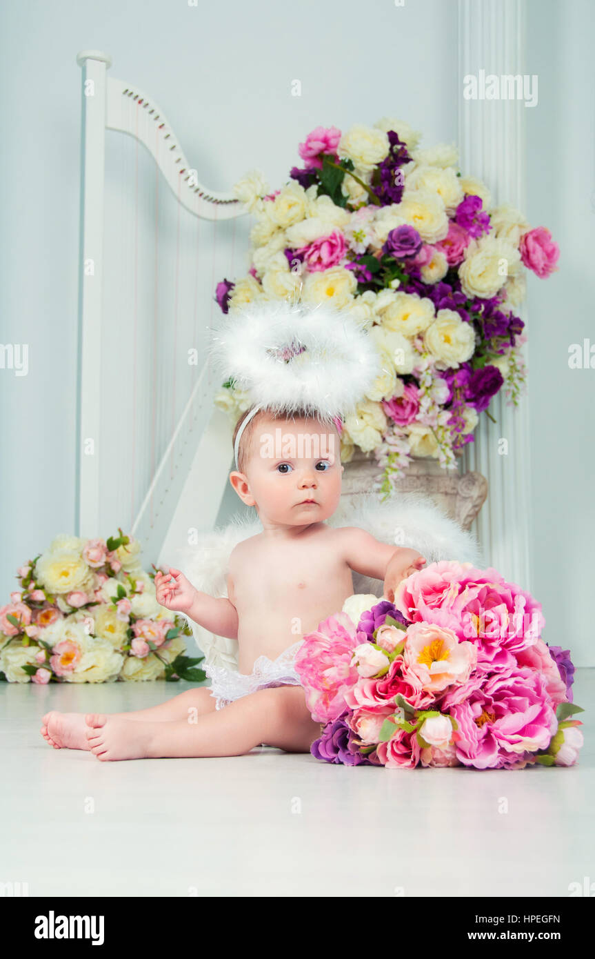 Little angel smiling and happy sitting on the background of flowers and ...