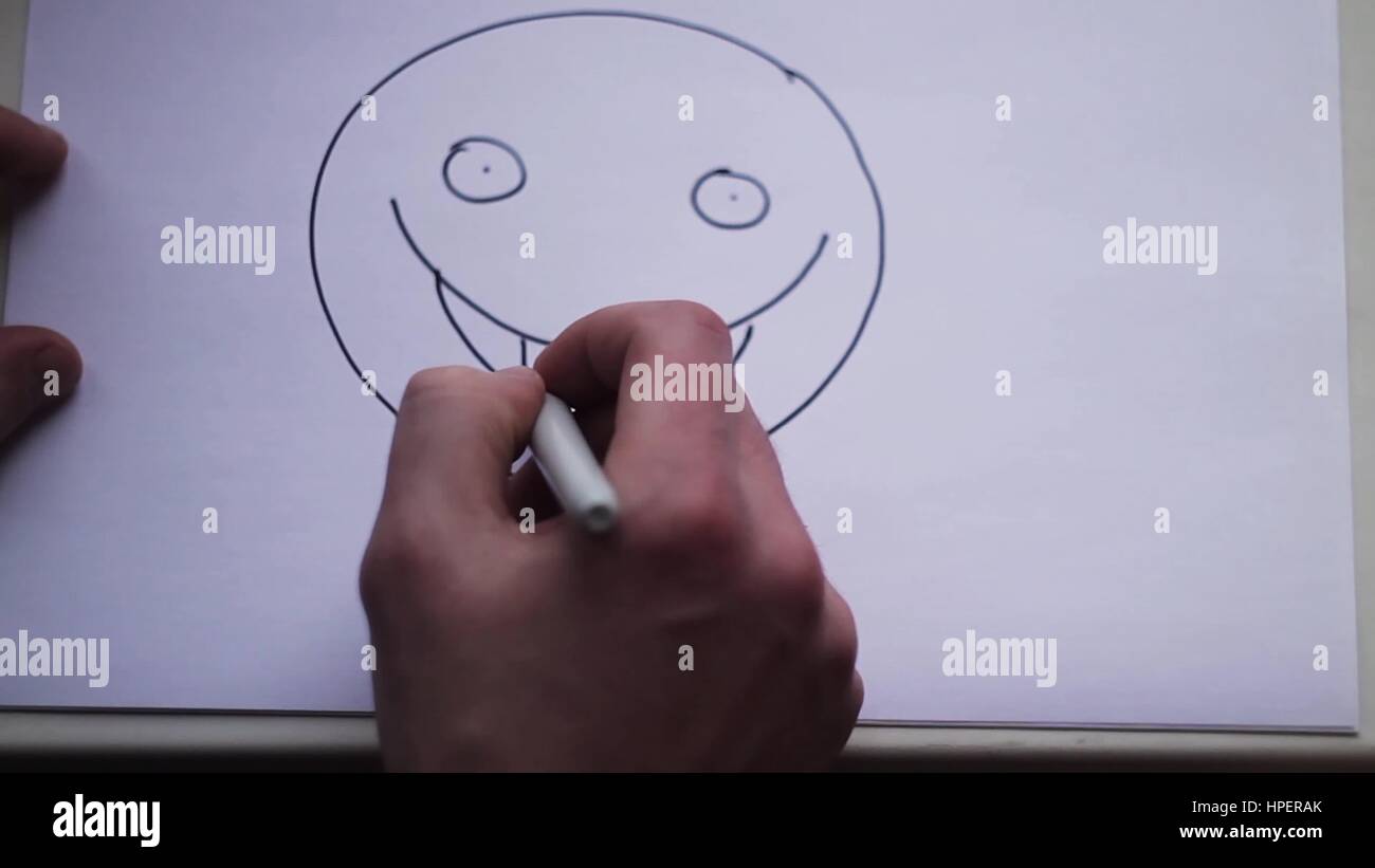 the hand of the young man draws a smiley face on a white sheet of paper ...
