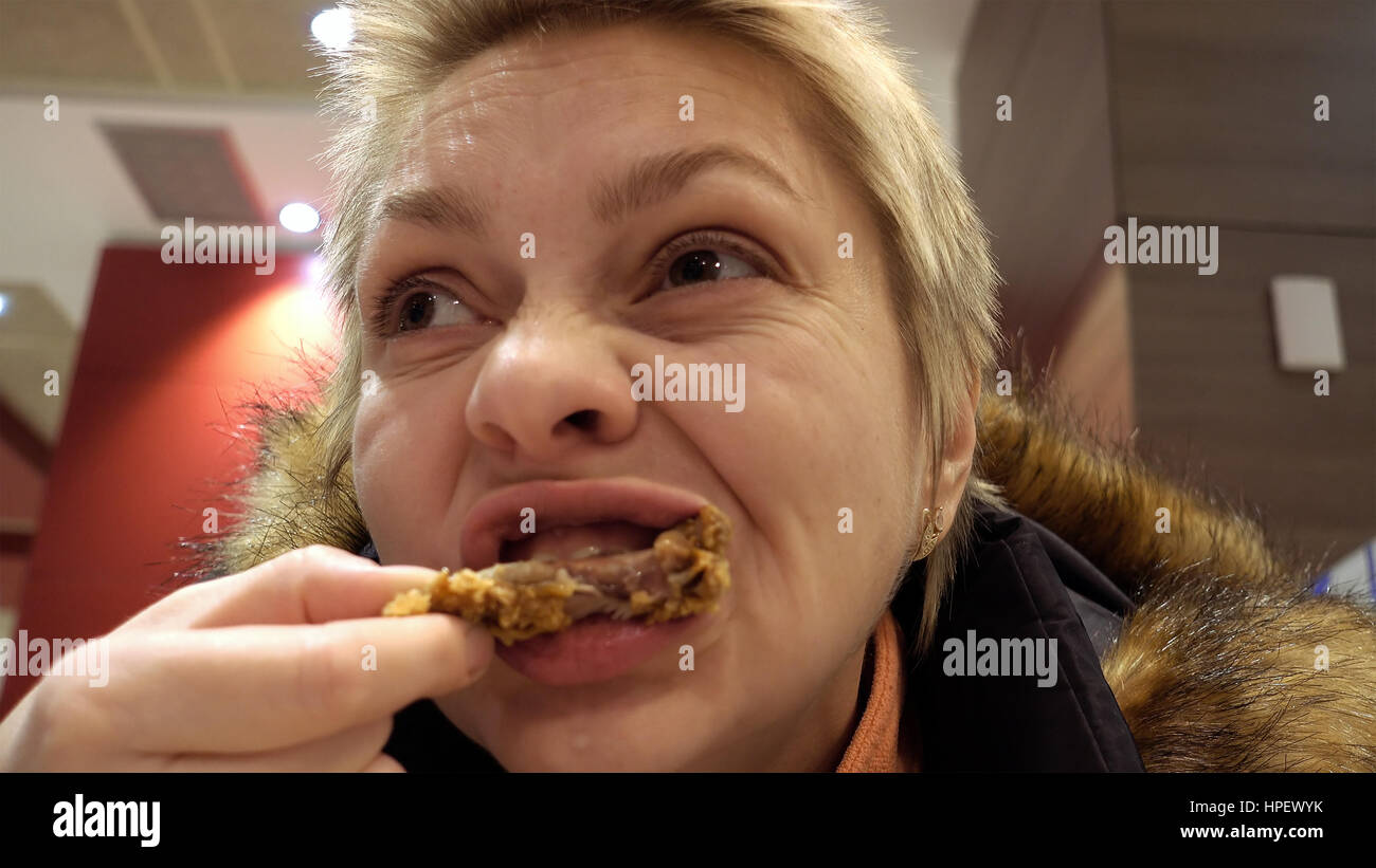 Woman expressively eats chicken in fast food restaurant. Face closeup ...