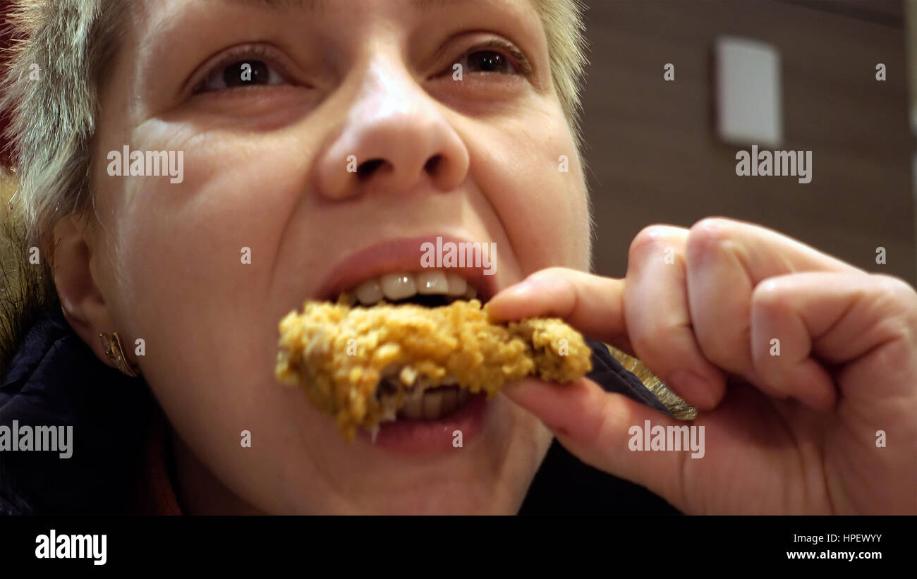 Woman expressively eats chicken in fast food restaurant. Face closeup ...