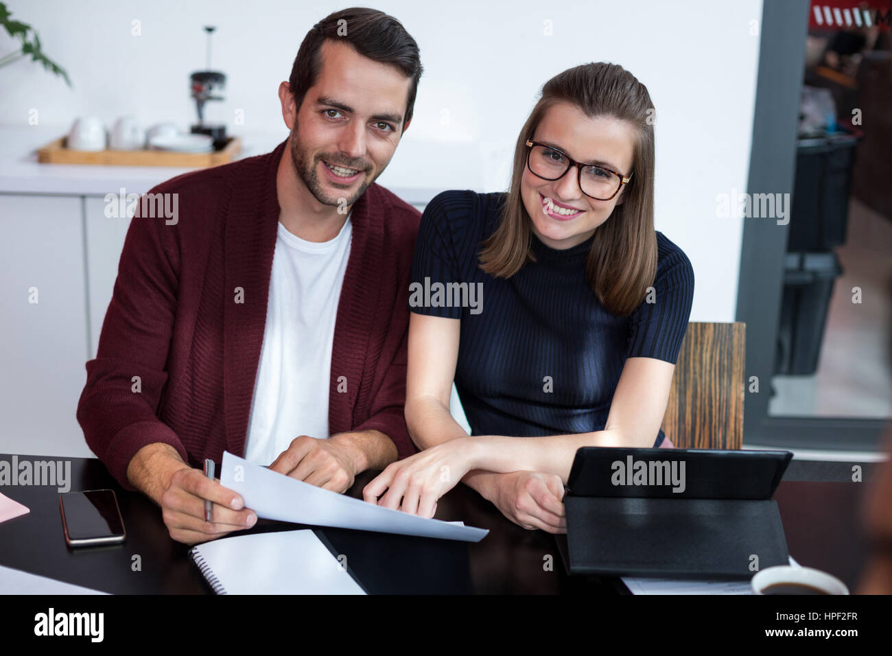 Smiling business executives discussing over digital tablet and document in meeting at office ...