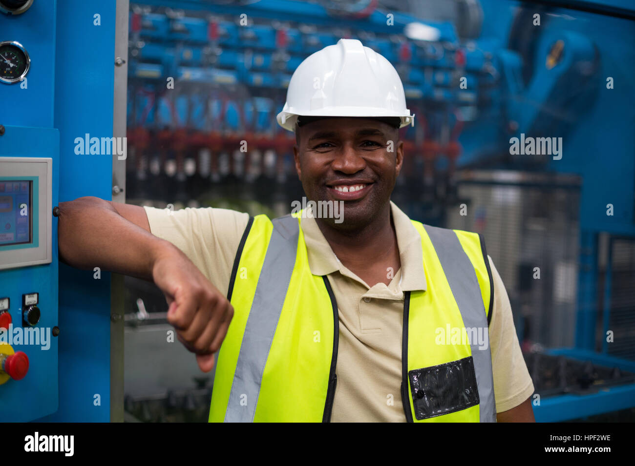 Portrait of smiling factory worker leaning on machine control cabinet ...