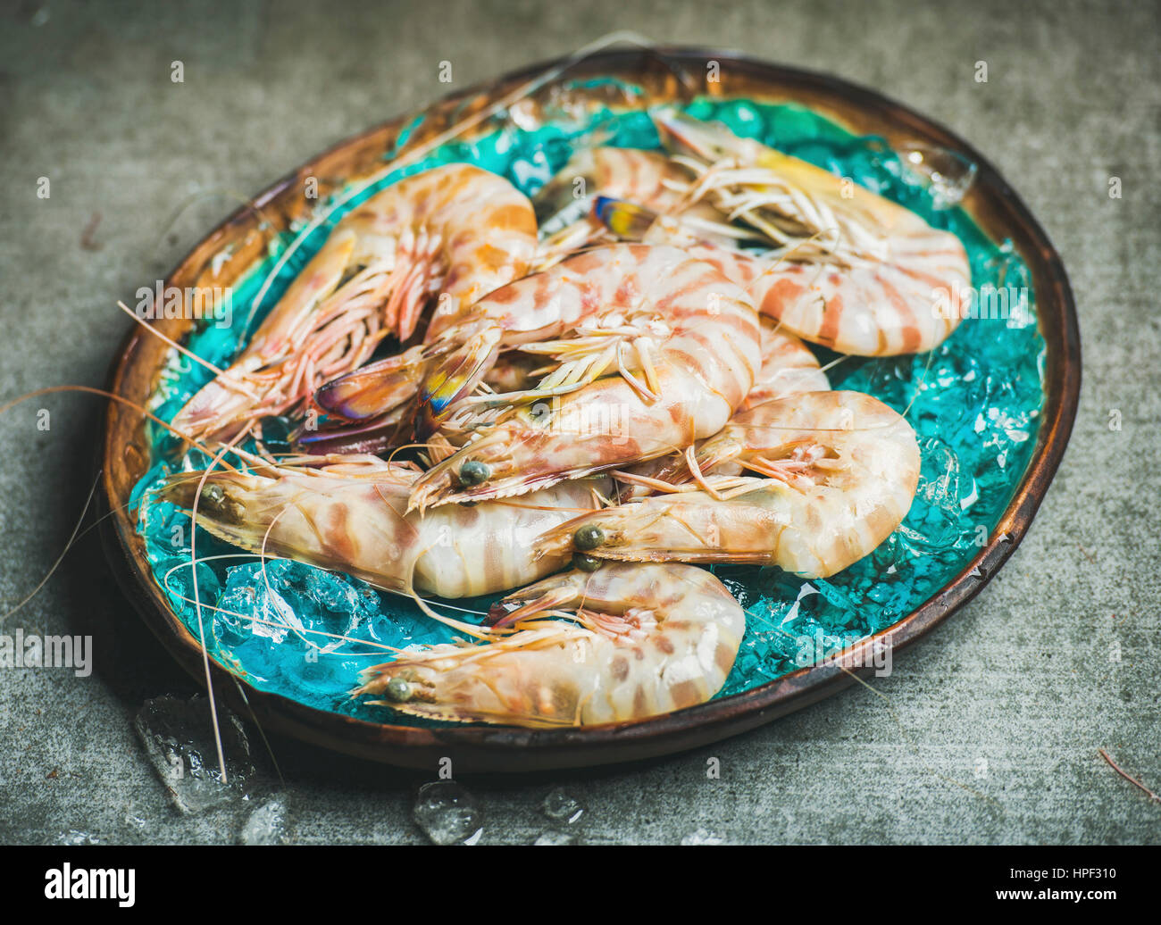 Raw uncooked tiger prawns on chipped ice in turquoise blue tray over ...