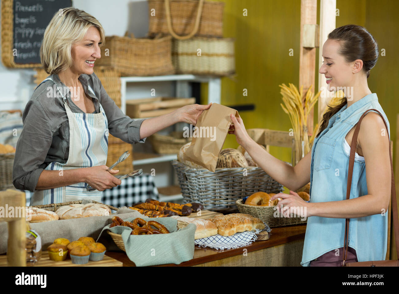 Smiling female customer receiving a parcel from bakery staff at counter ...