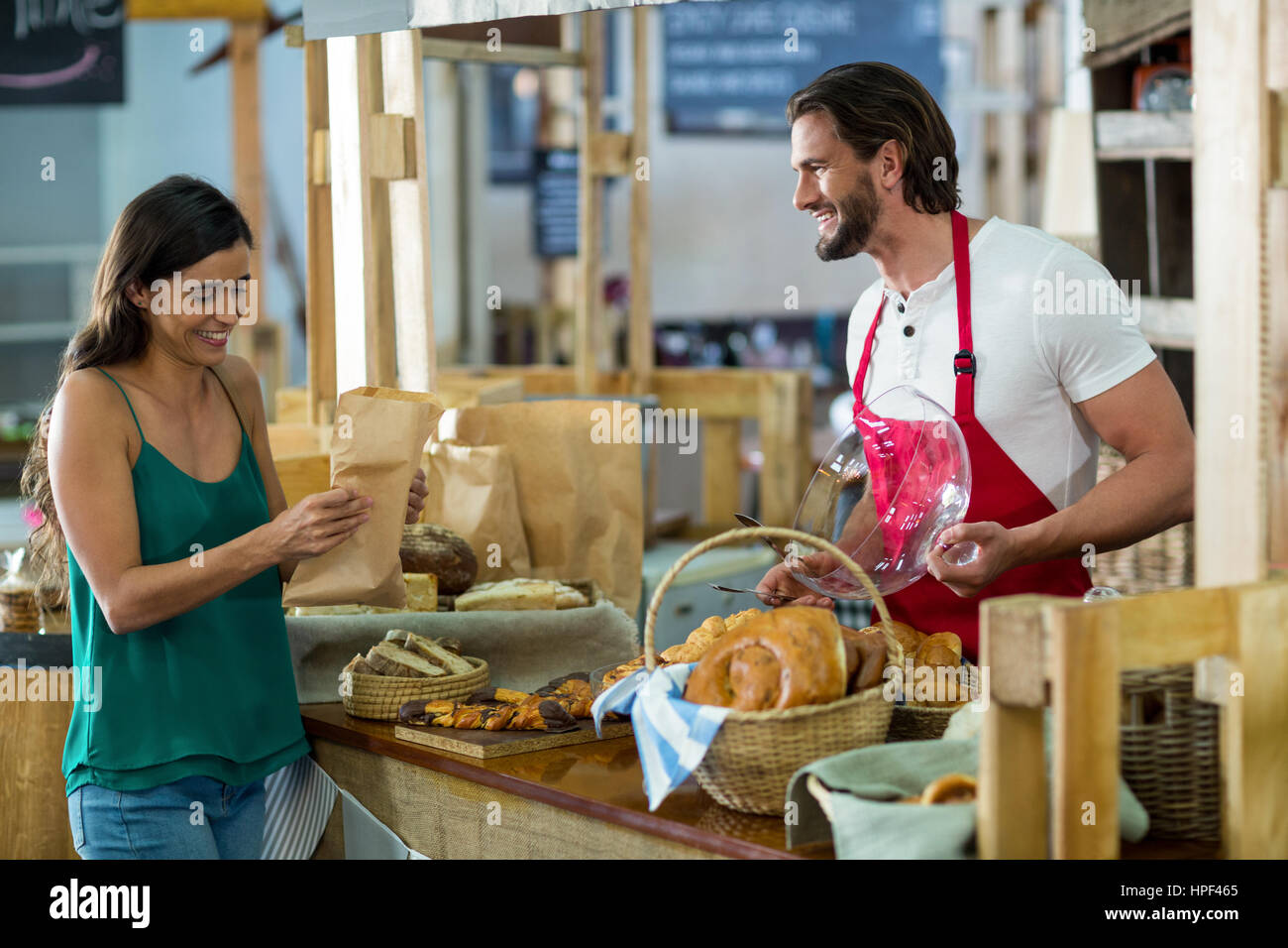 Smiling female customer receiving a parcel from bakery staff at counter ...