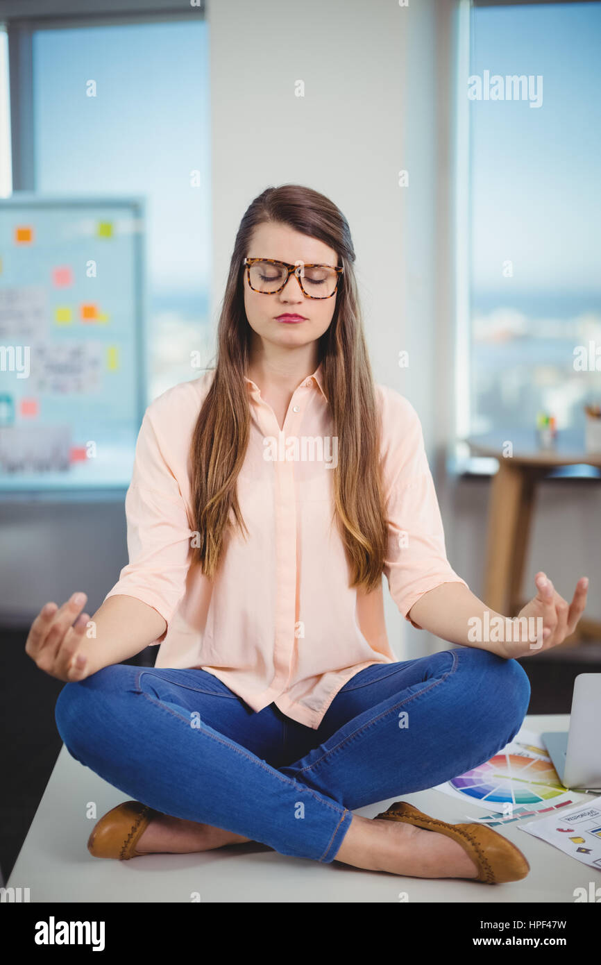Female graphic designer sitting on table and meditating in office Stock ...