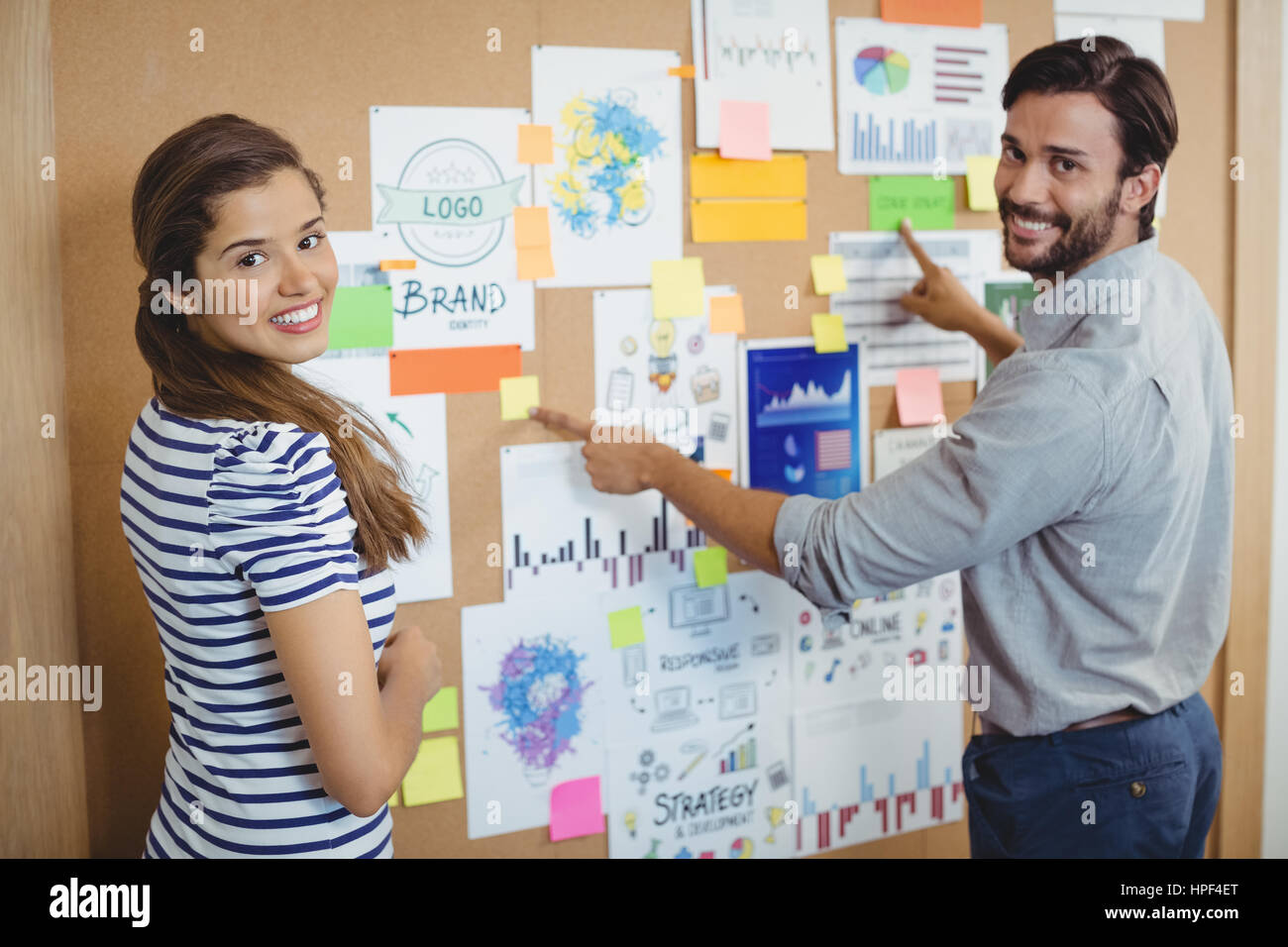 Portrait of two business executives discussing over bulletin board in ...