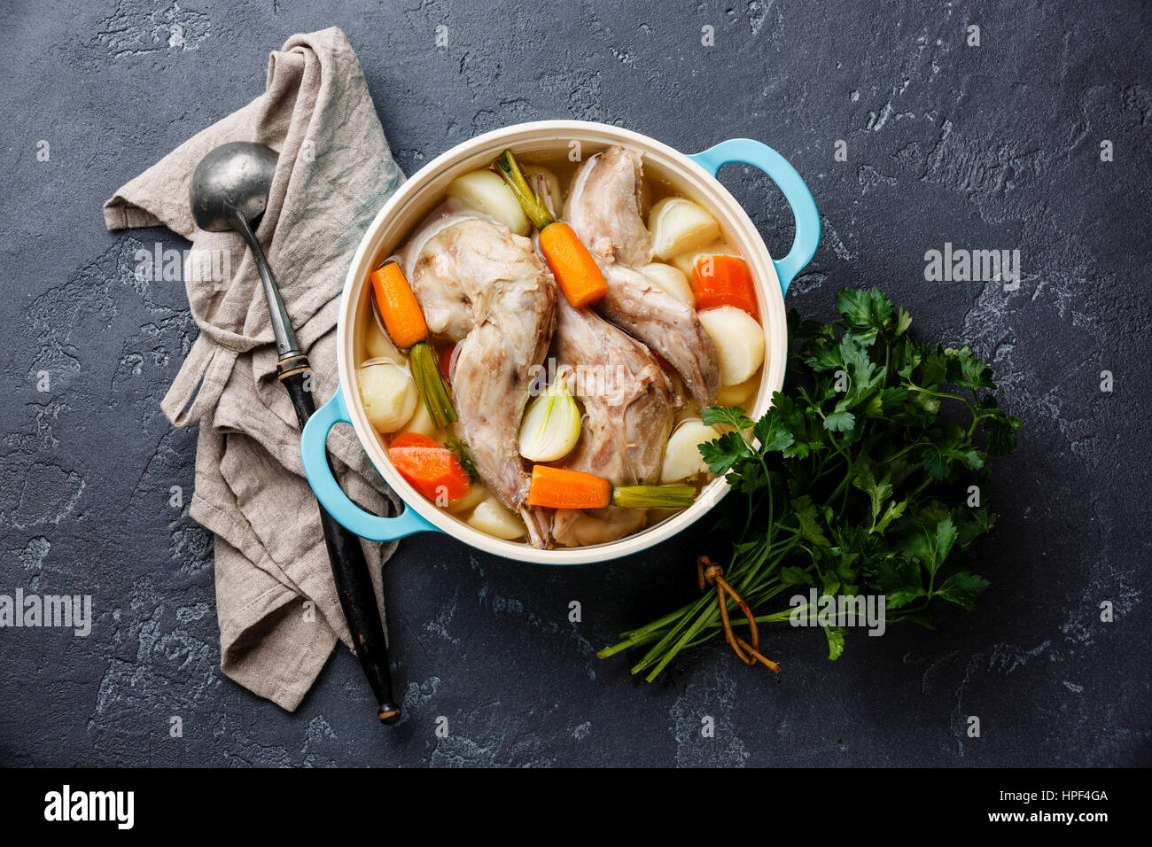 Stewed rabbit with potatoes and carrot in cast iron pot on dark stone ...