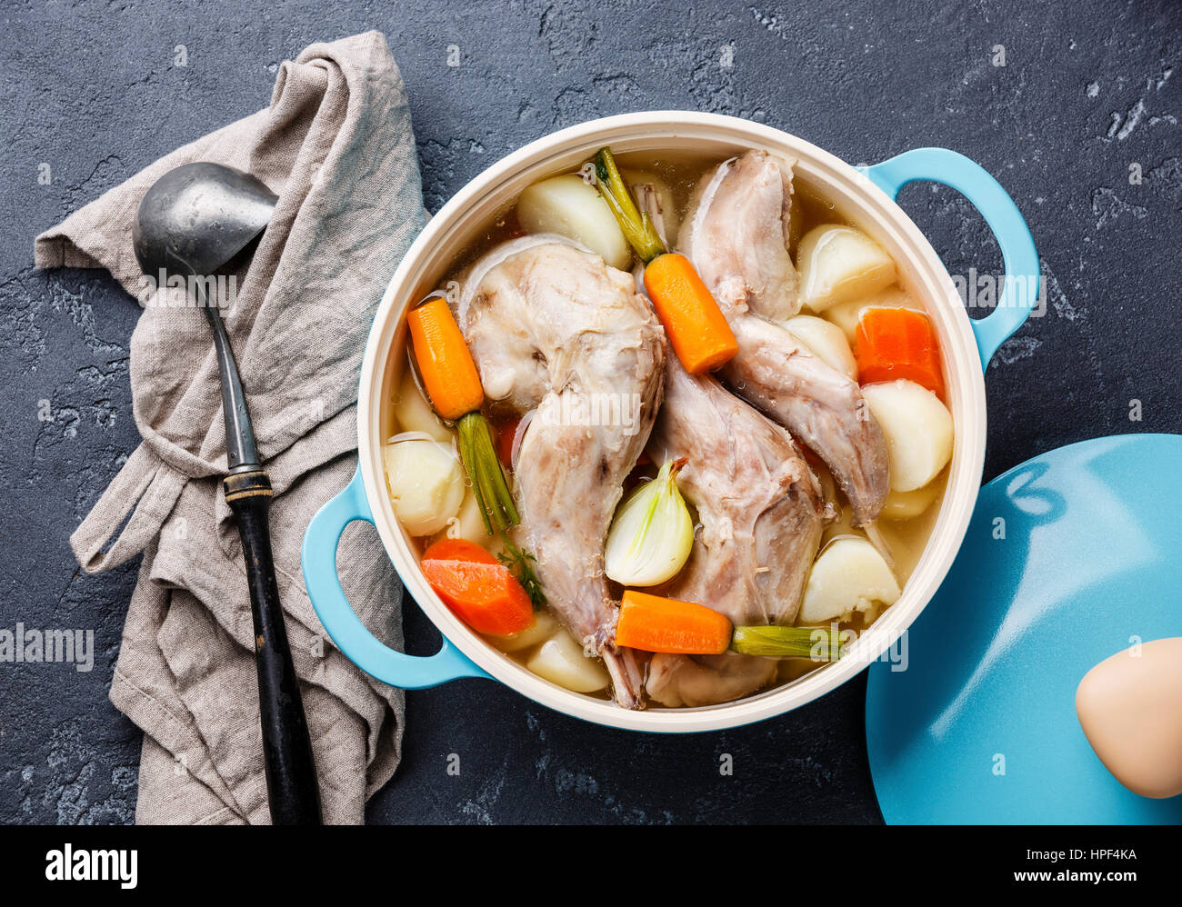 Stewed rabbit with potatoes and carrot in cast iron pan on dark stone ...