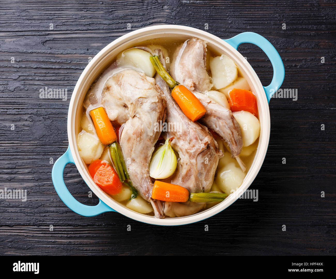 Stewed rabbit with potatoes and carrot in cast iron pan on black burned ...