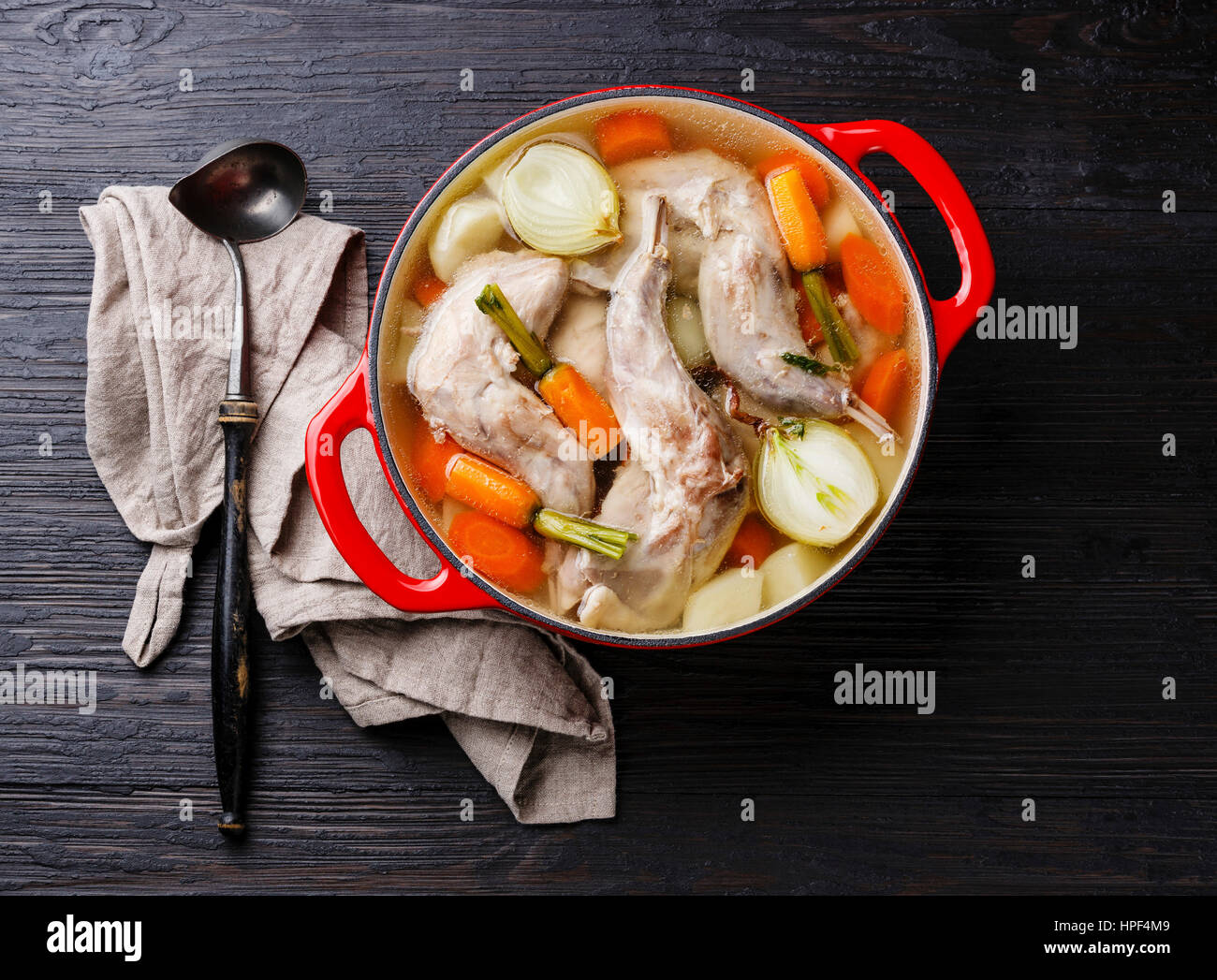 Stewed rabbit with potatoes and carrot in cast iron pan on black burned ...
