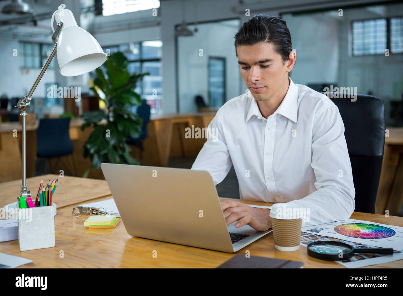 Man using laptop at desk in creative office Stock Photo - Alamy