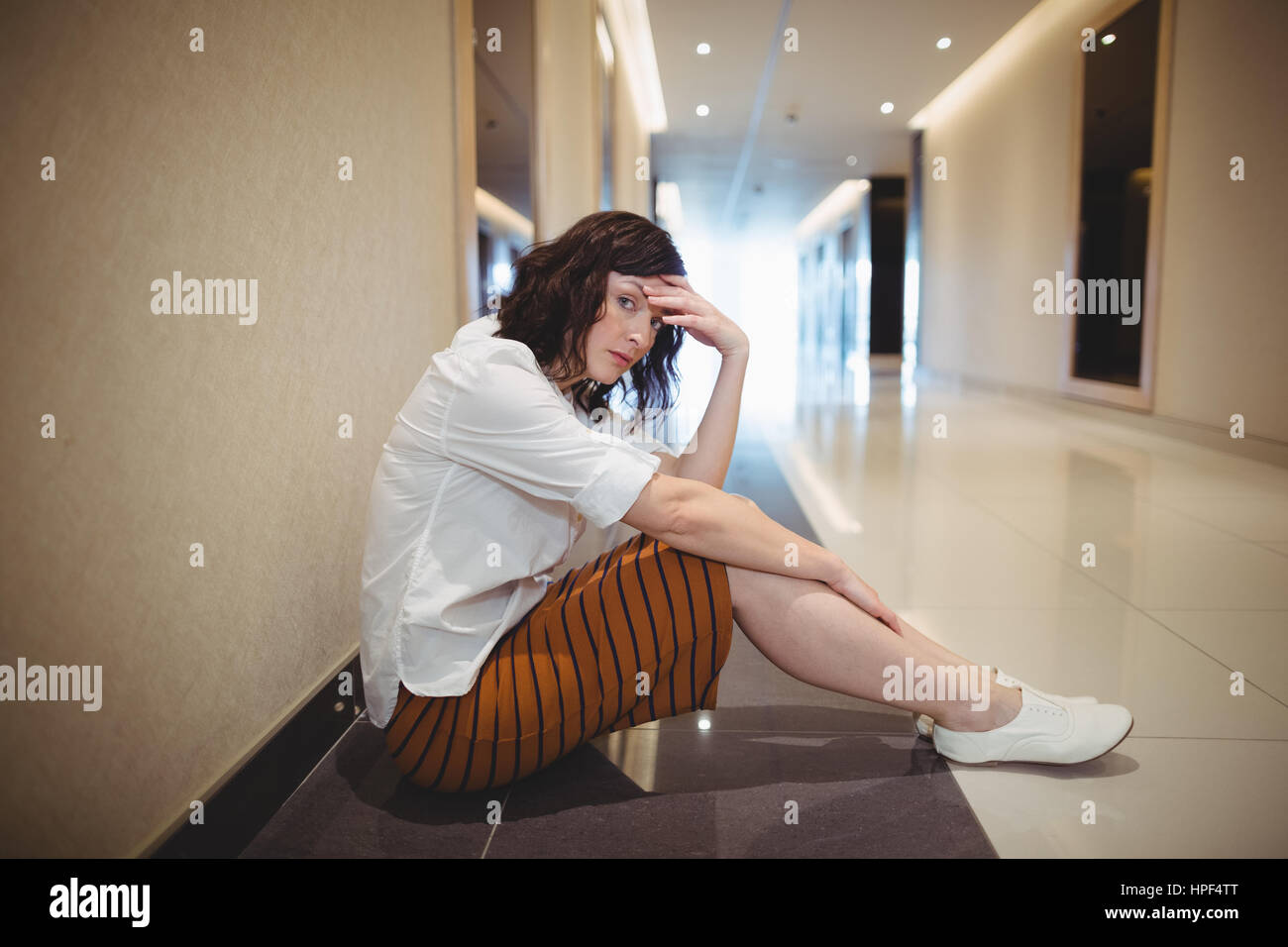 Portrait of sad female business executive sitting in corridor in office ...