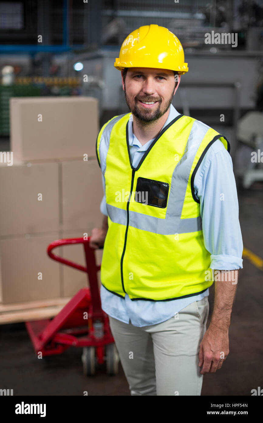 Portrait of factory worker pulling trolley of cardboard boxes in ...