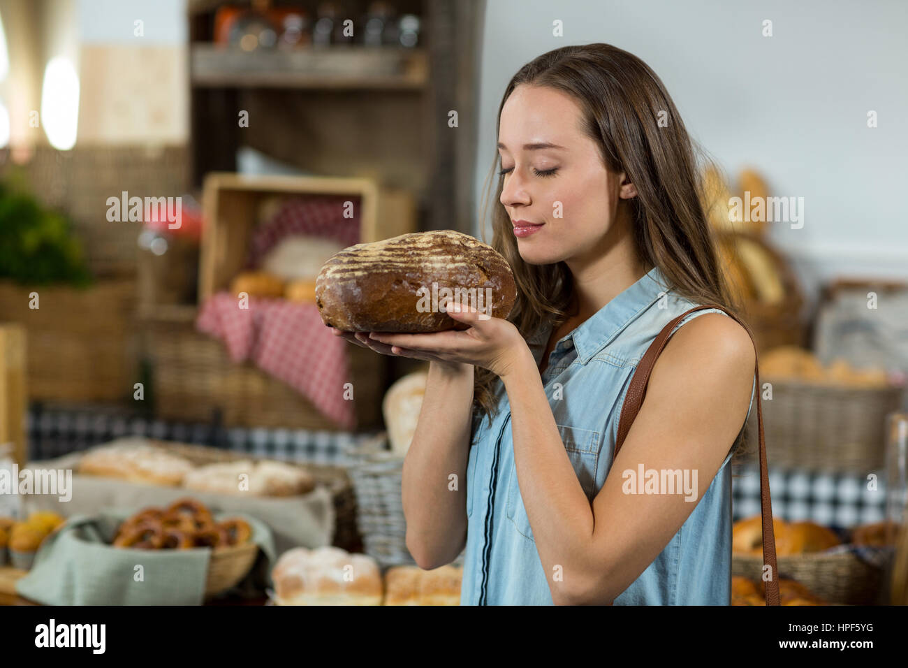 Smiling woman smelling a round loaf of bread at counter in bake shape ...