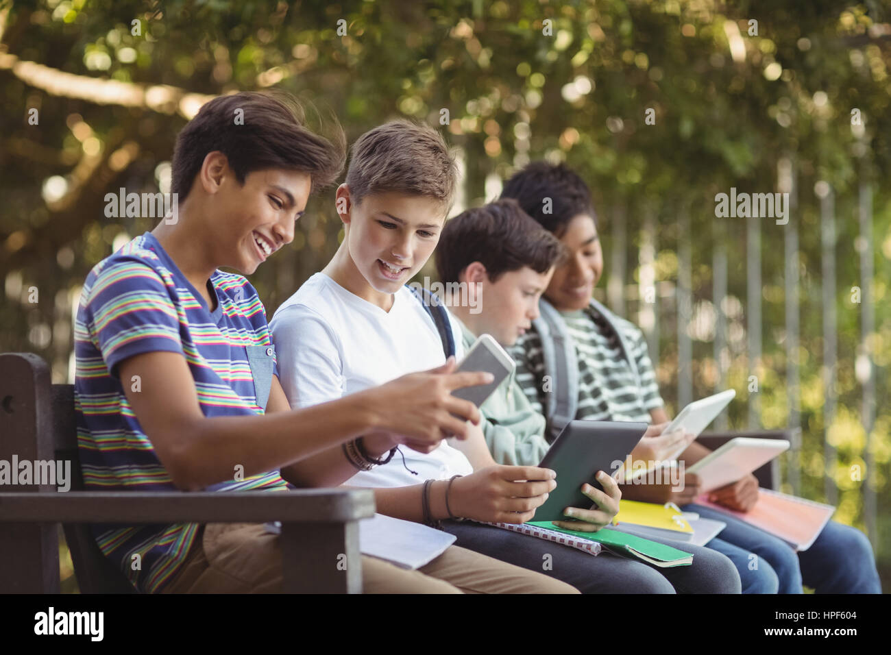 School kids using mobile phone and digital tablet on bench in school ...