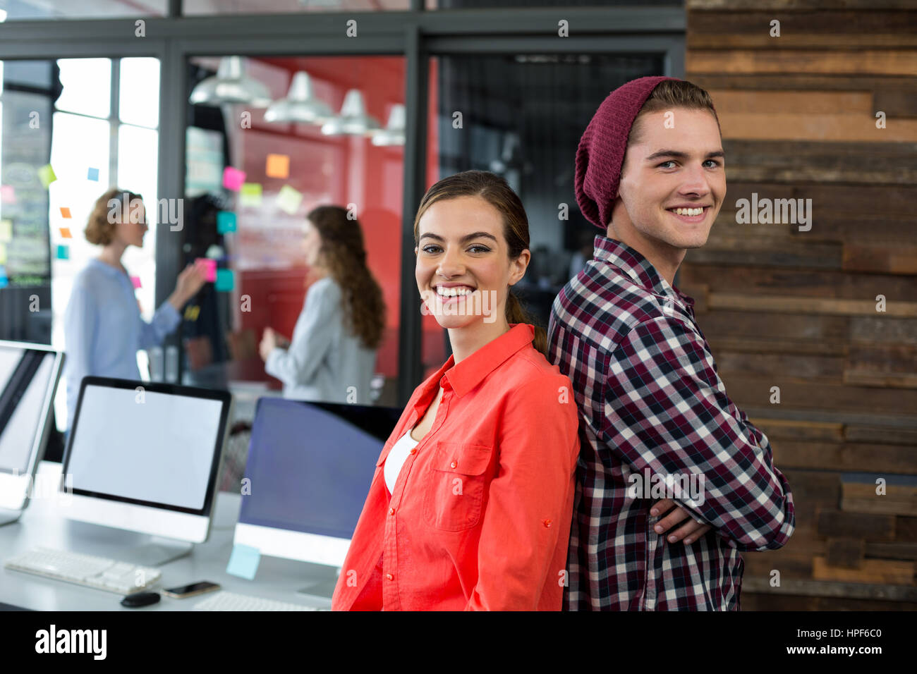 Portrait of smiling business executive standing back to back in office ...