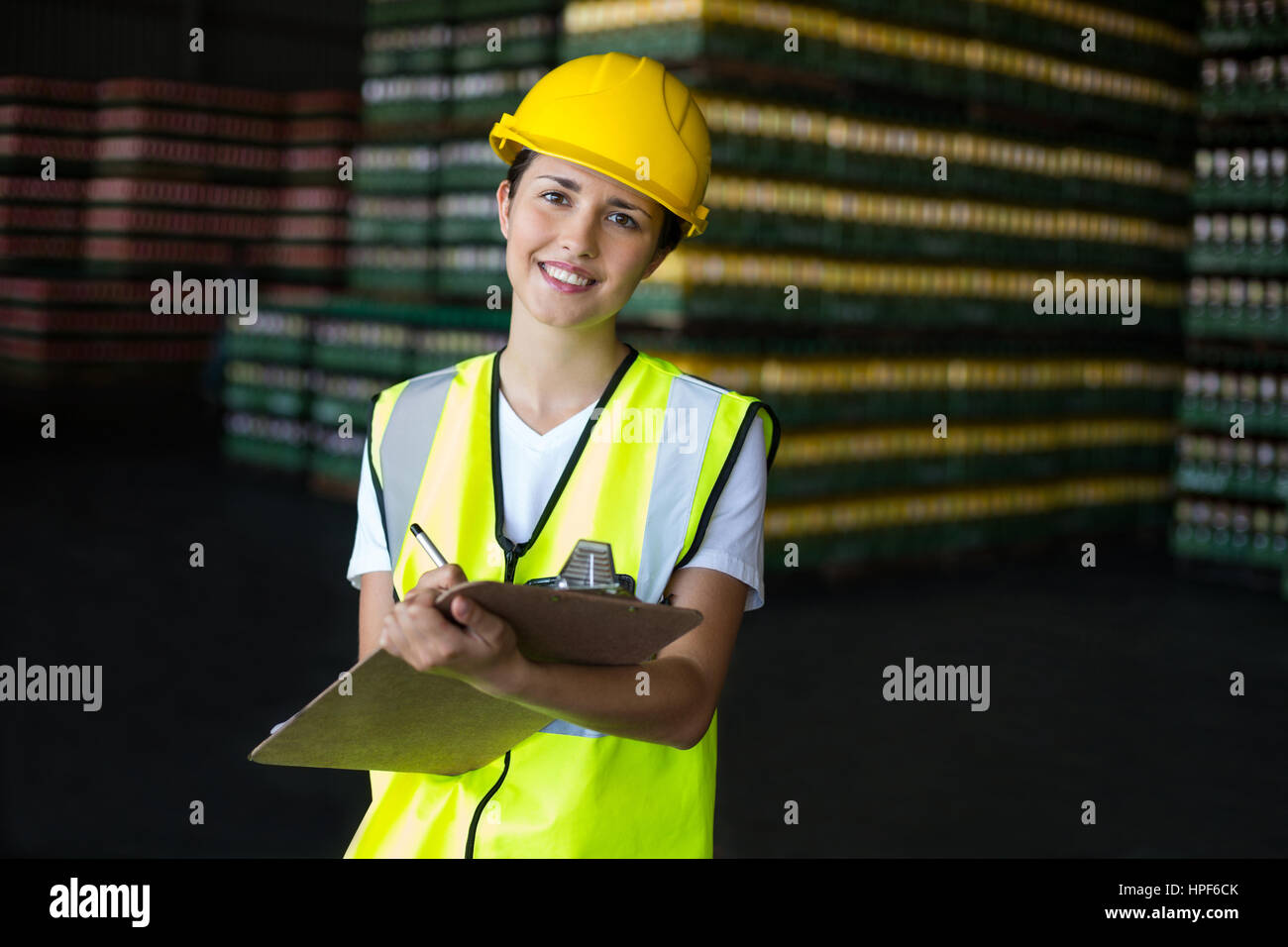 Portrait of smiling female factory worker writing on clipboard in ...