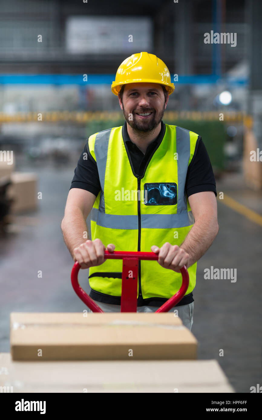 Portrait of smiling factory worker pulling trolley of cardboard boxes ...