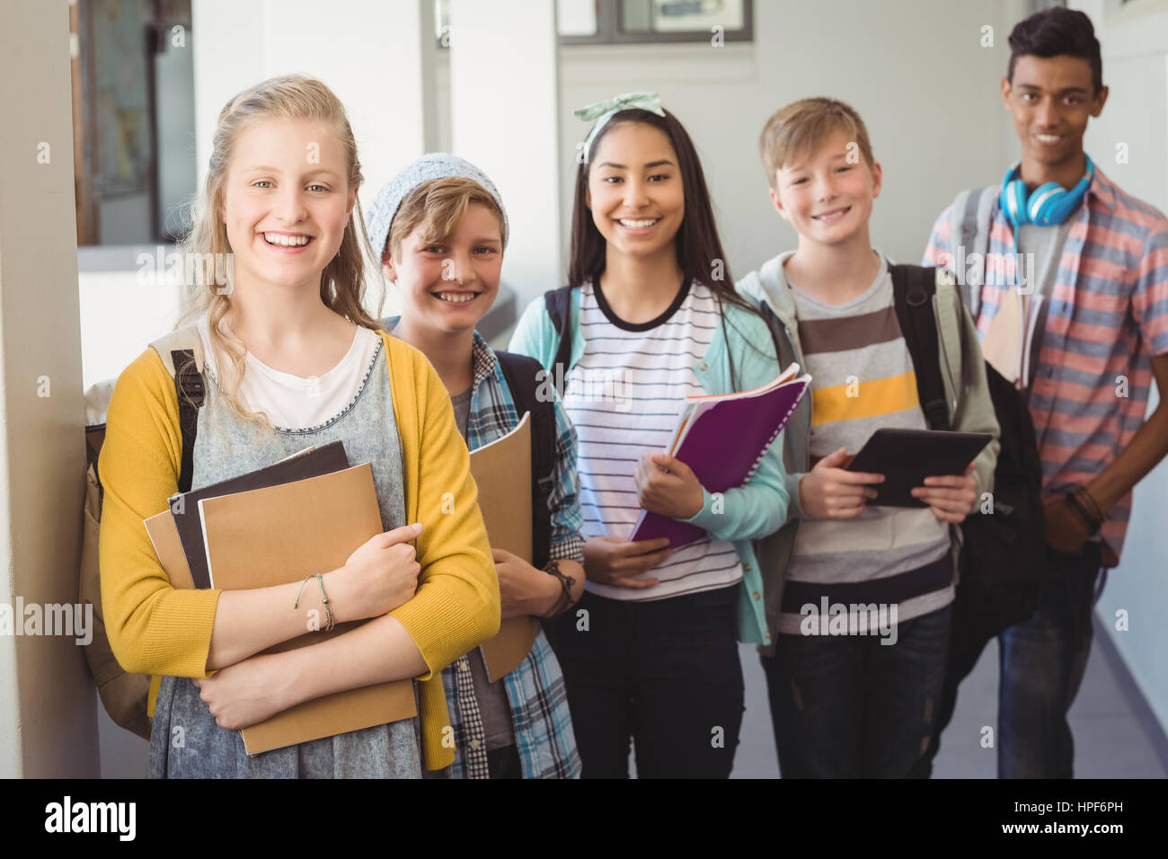 Group of smiling students standing with notebook in corridor at school ...