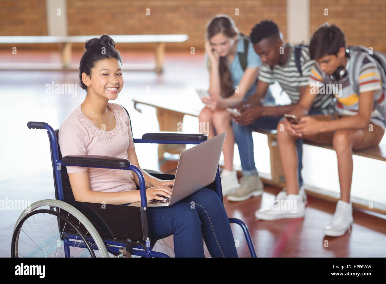 Portrait of disabled schoolgirl using laptop with classmates in ...