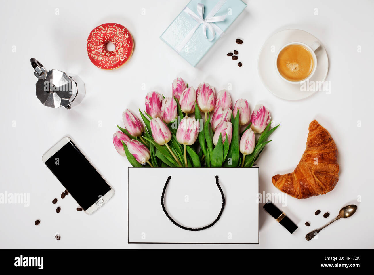 Top view of spring flowers, coffee, mobile phone, croissants, gift and ...