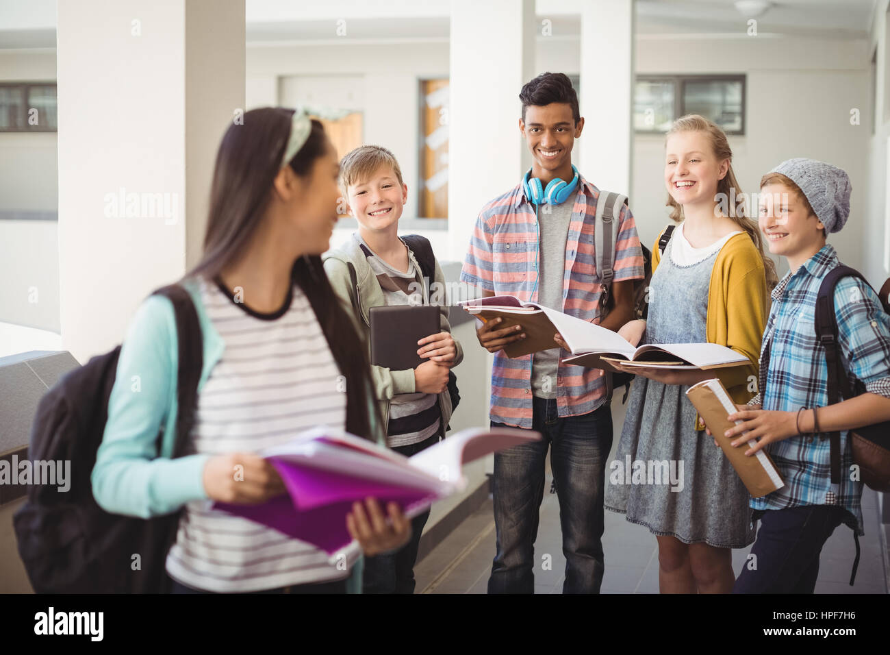 Group of smiling students standing with notebook in corridor at school ...