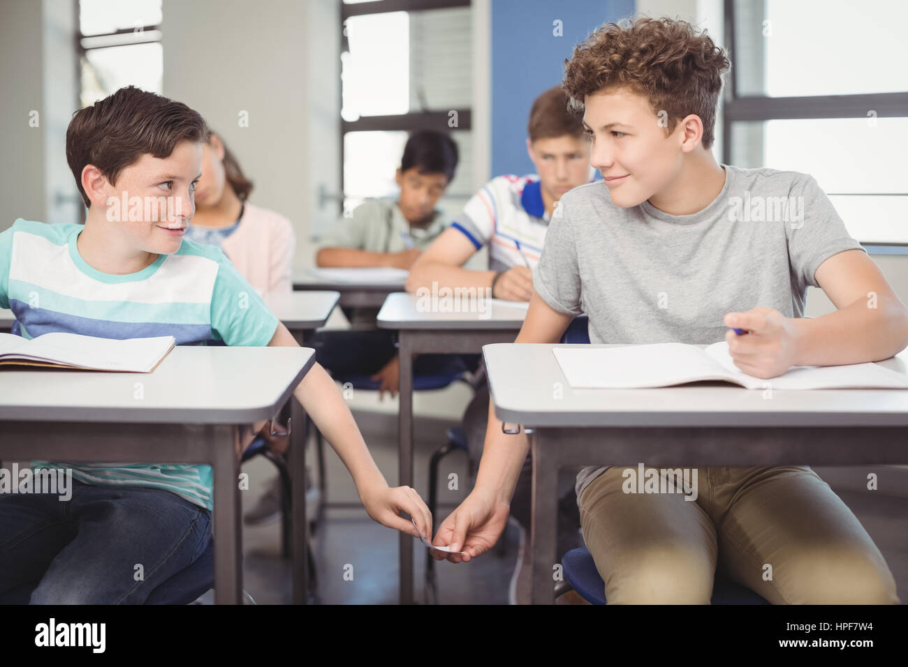 School students passing a chit in a secretive way inside the classroom ...