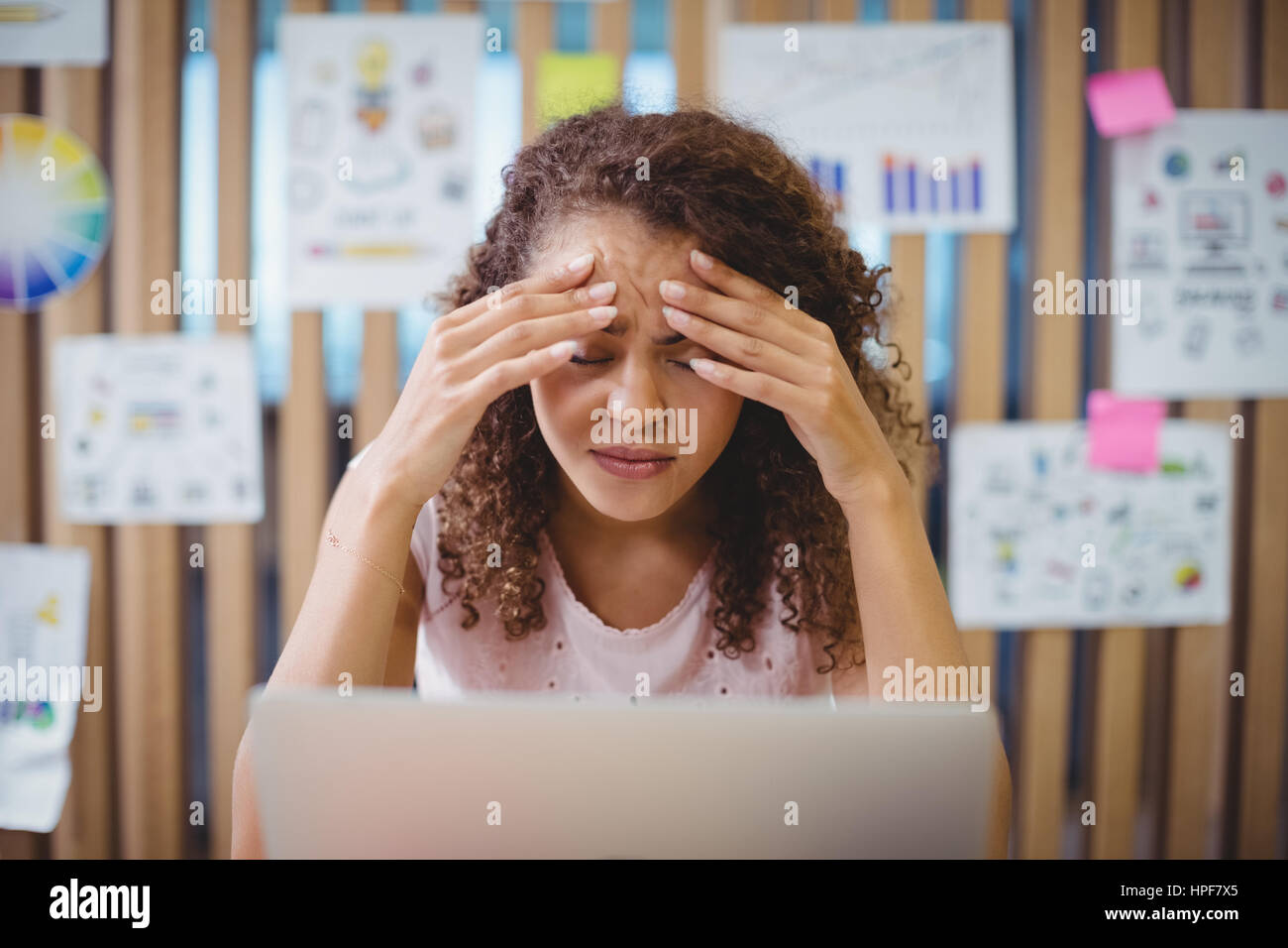 Frustrated female graphic designer with laptop siting at desk in office ...