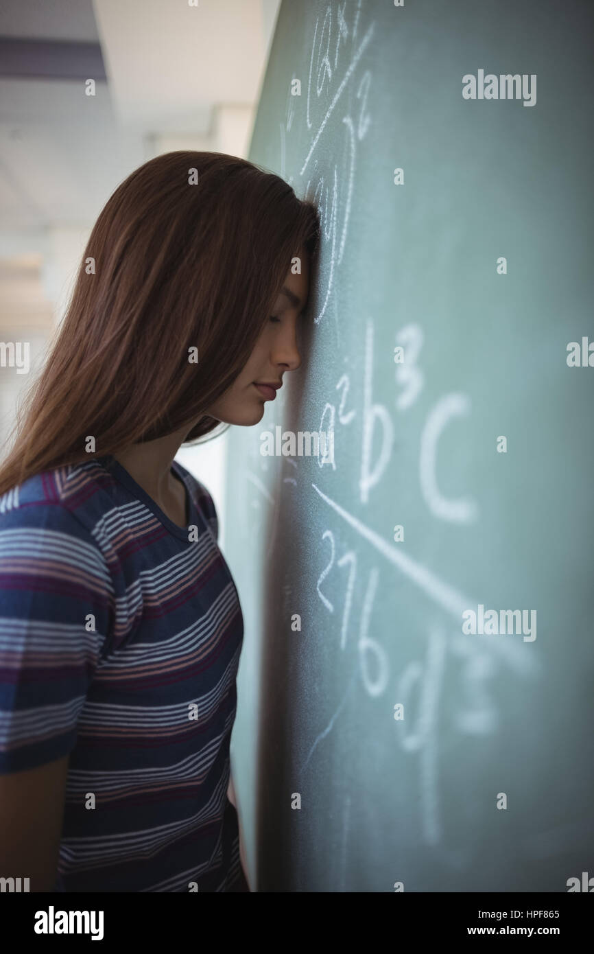 Tired schoolgirl standing with closed eyes near chalkboard in classroom ...