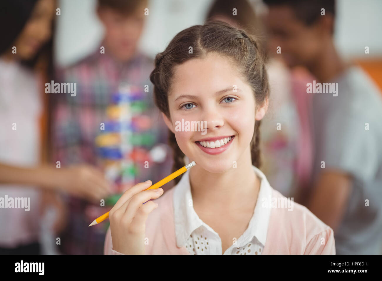 Portrait of smiling schoolgirl standing with pencil in classroom at ...