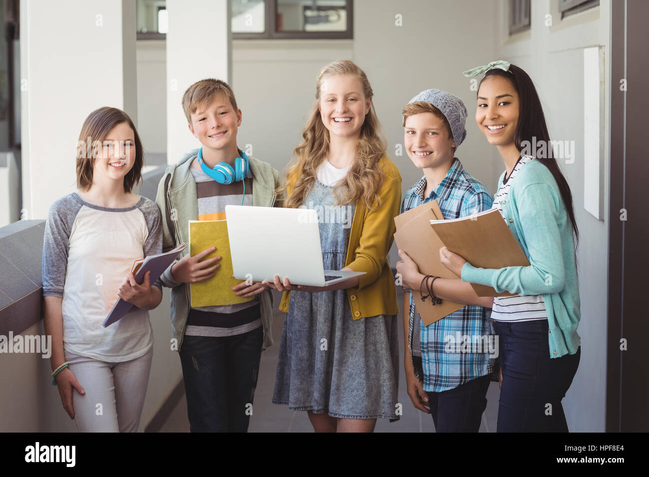 Portrait of smiling school students using laptop in corridor at school ...