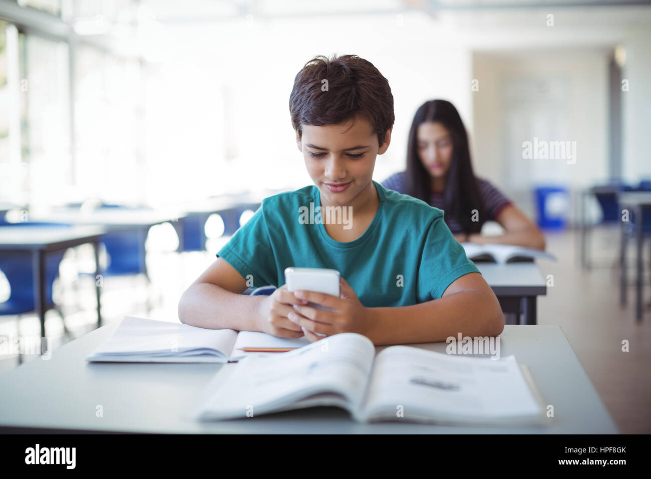 Schoolboy using mobile phone while studying in classroom at school ...