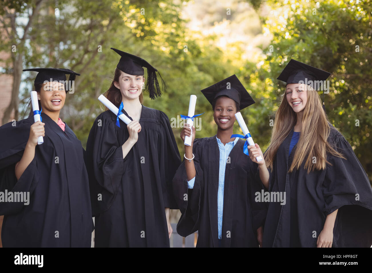Portrait of graduate school kids standing with degree scroll in campus ...