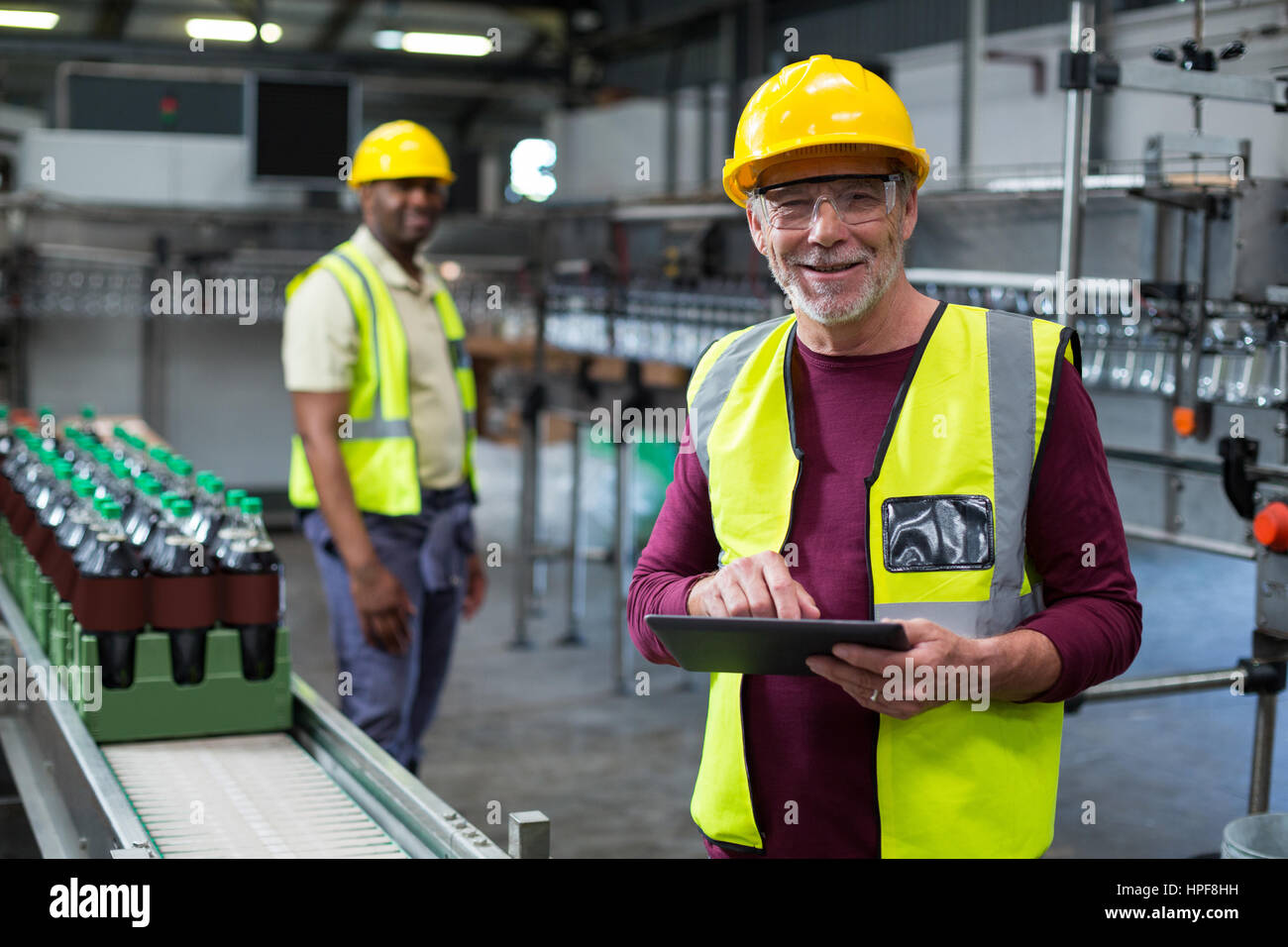 Smiling factory worker with digital tablet standing near the production ...