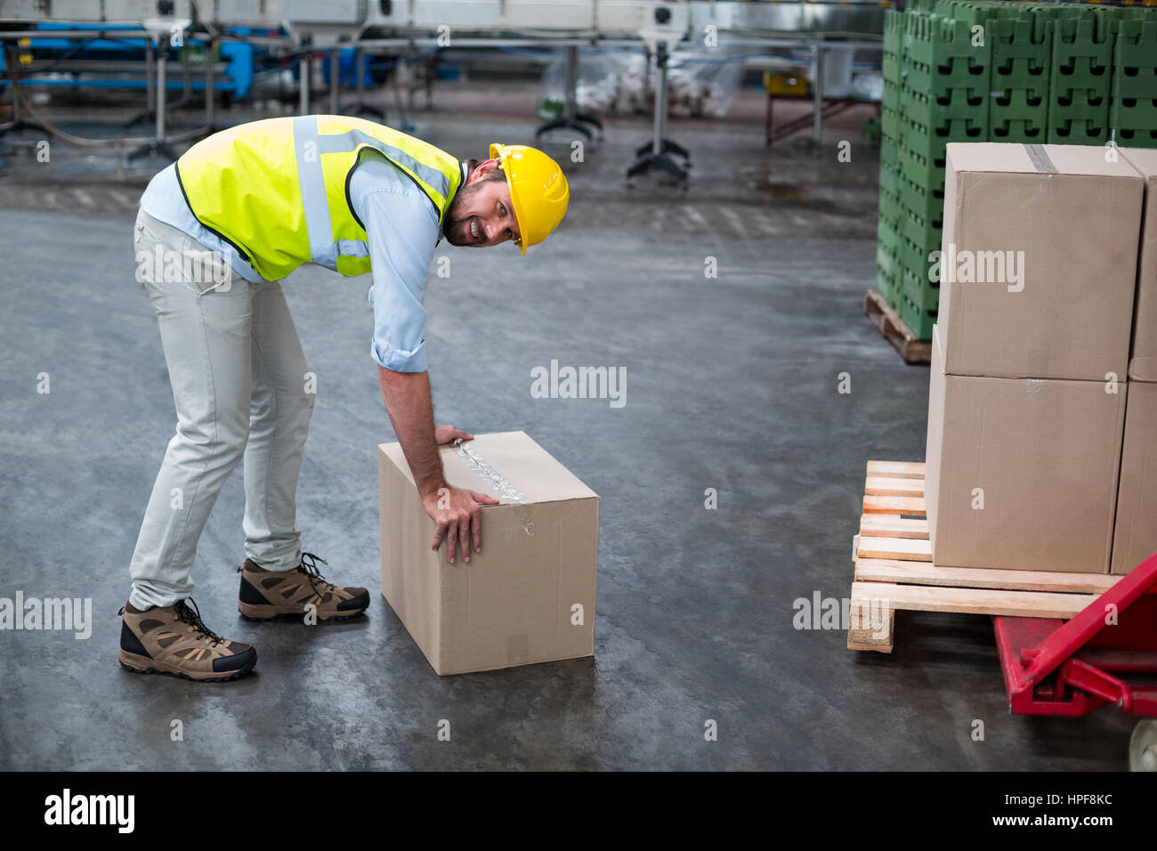 Portrait of factory worker picking up cardboard boxes in factory Stock ...