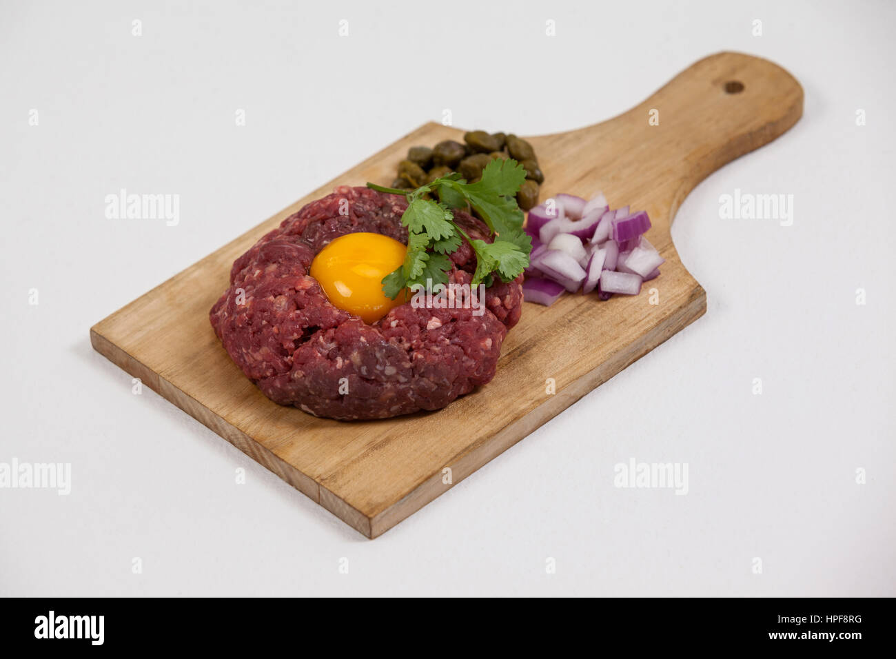 Beef patty, onions and olives on wooden board against white background ...