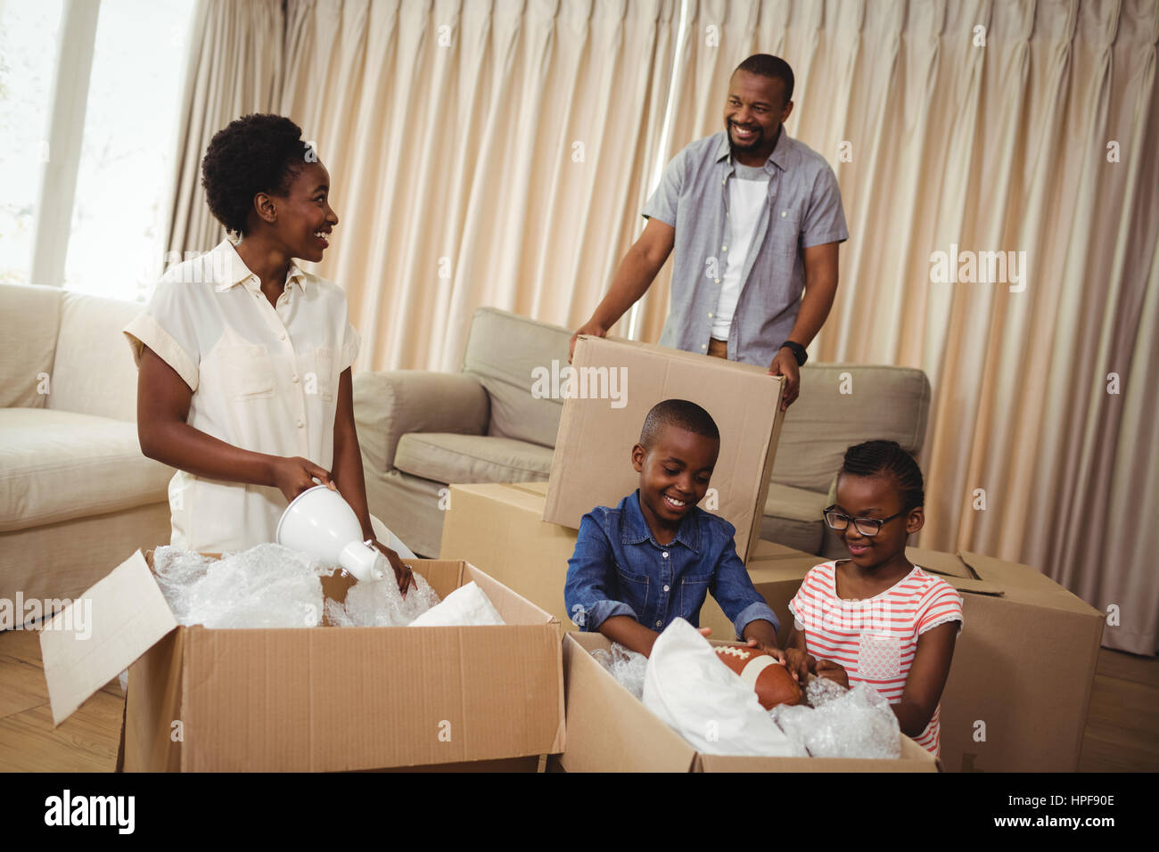 Parents and kids opening cardboard boxes in living room at home Stock ...