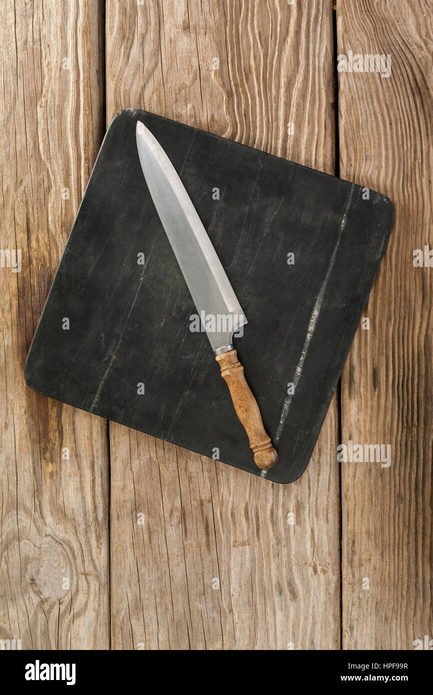 Knife on black slate plate against wooden background Stock Photo - Alamy