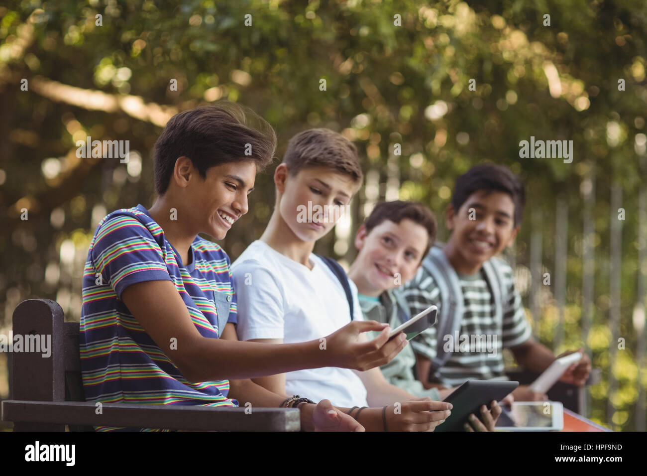 School kids using mobile phone and digital tablet on bench in school ...