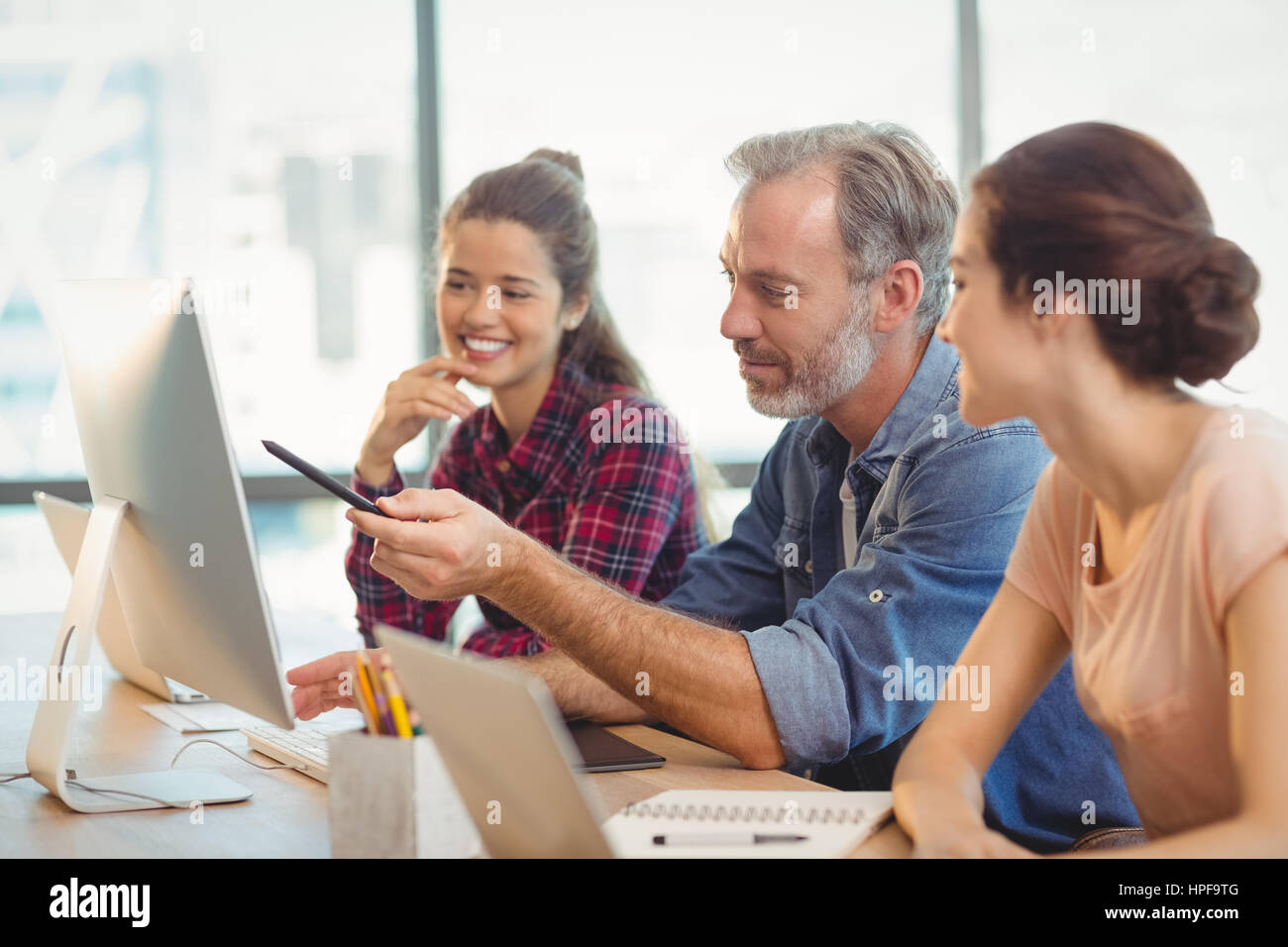 Team of graphic designers discussing over computer at desk in office ...