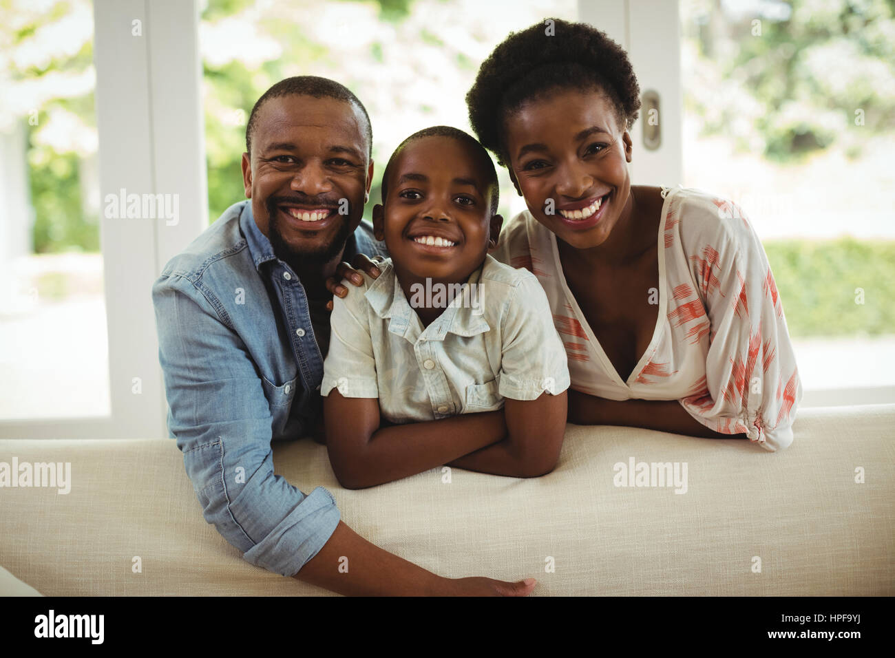Portrait of parents and son leaning over sofa in living room at home ...