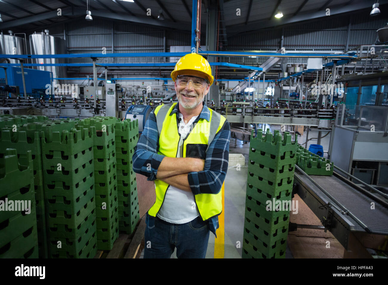 Portrait of male factory worker standing with arms crossed in drinks ...