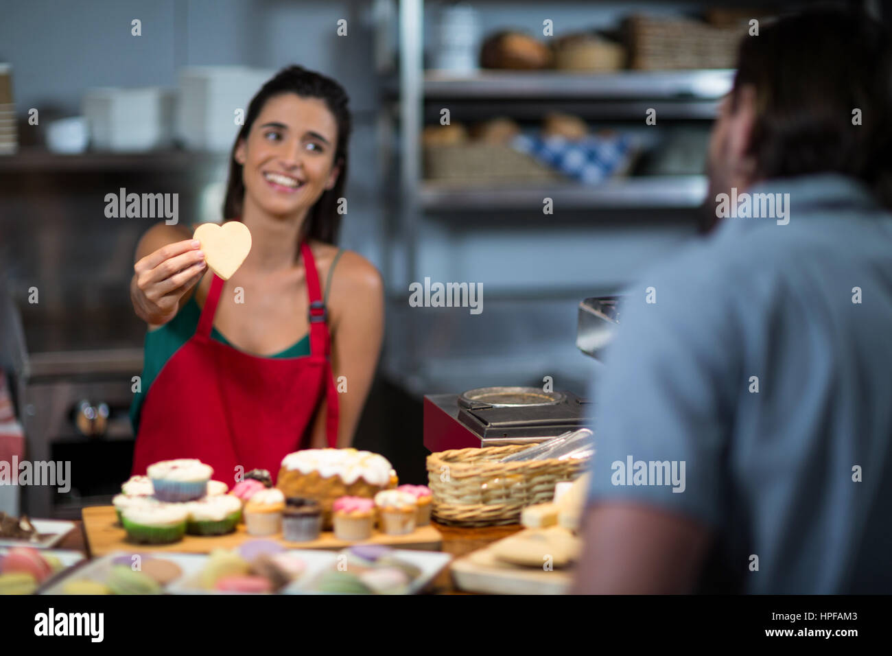 Smiling female staff giving heart shape cookie to customer at counter ...