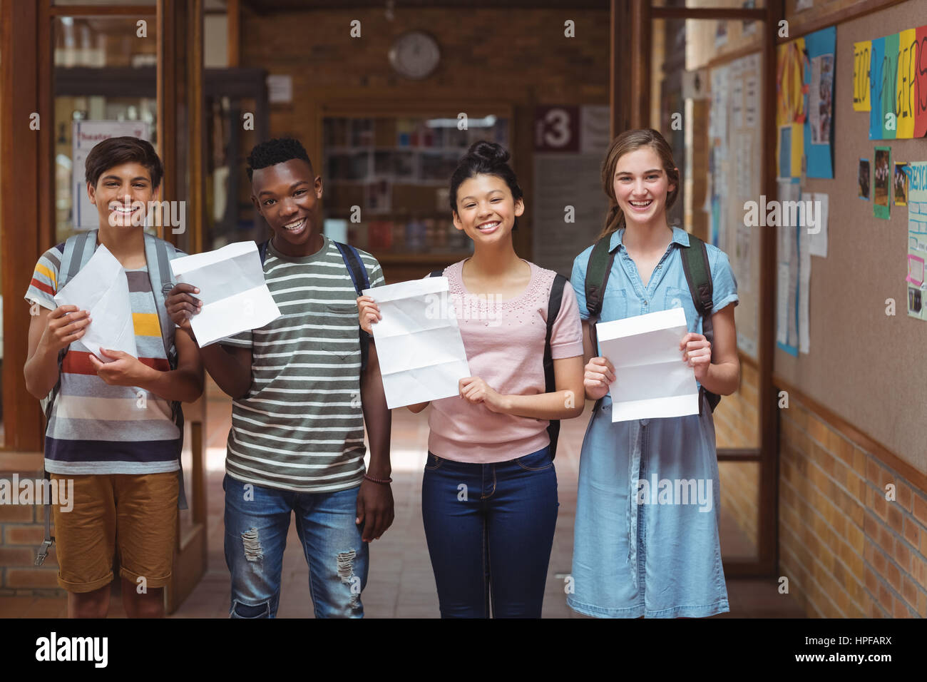Portrait of happy classmates holding grade cards in corridor at school ...