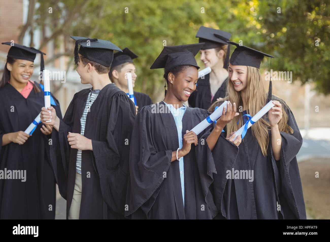 Smiling graduate school kids standing with degree scroll in campus at ...