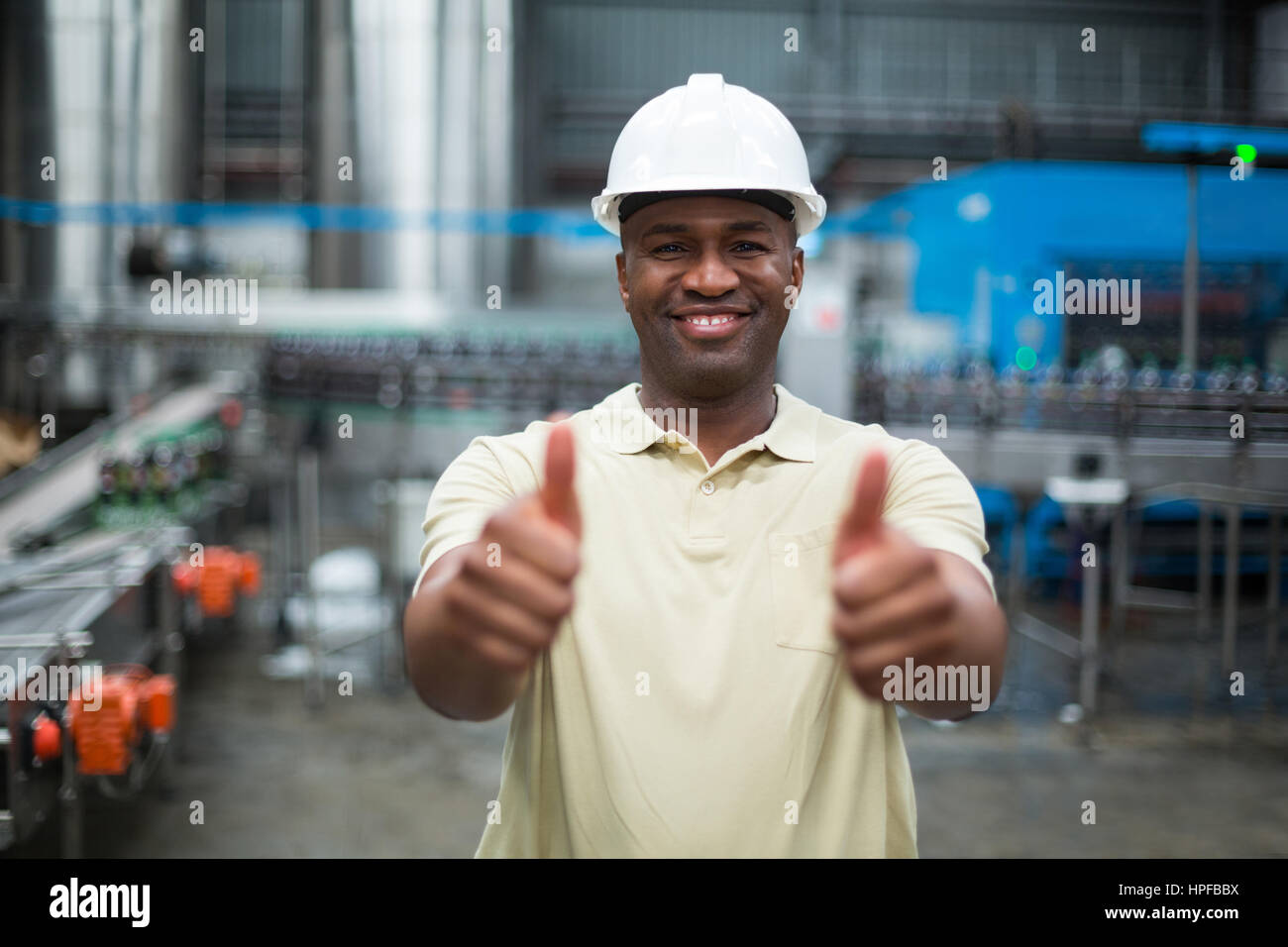Portrait of happy factory worker showing his thumbs up in drinks ...