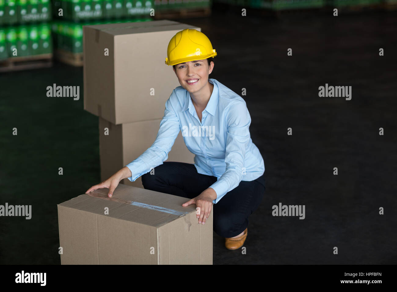 Portrait of female factory worker picking up cardboard boxes in factory ...